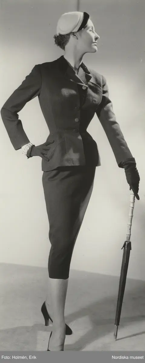 Modell i dräkt, handskar, hatt och pumps med paraply i handen. Från ...