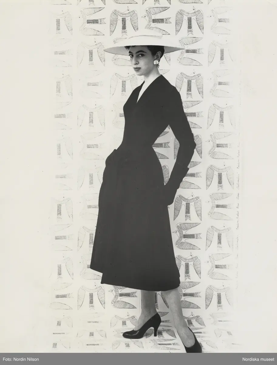 Modell i svart klänning, vit hatt och tecknad bakgrund. NK efter idé ...