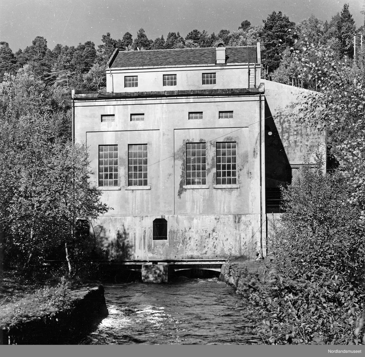 Heggmoen kraftstasjon, vannkanal i forgrunnen. Trær. - Nordlandsmuseet ...