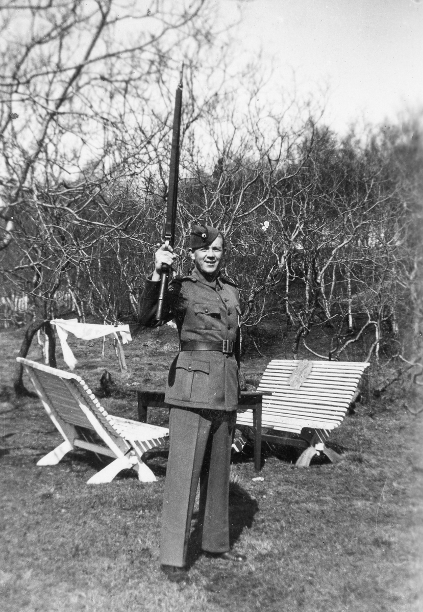 Soldat med gevær. Hagebenker i bakgrunnen. - Sør-Troms Museum / DigitaltMuseum