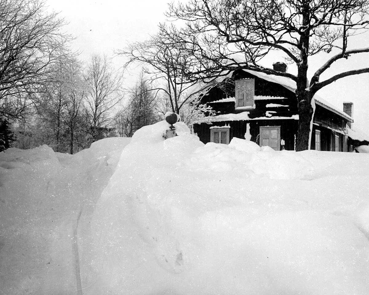 Vinterbilde med bolighus og hage rundt med portstolpe som stikker opp ...