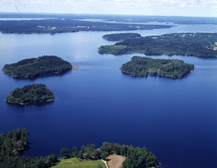 Färgfoto. Sjön Bolmen från väster med Bolmsö i bakgrunden. Man skymtar ...