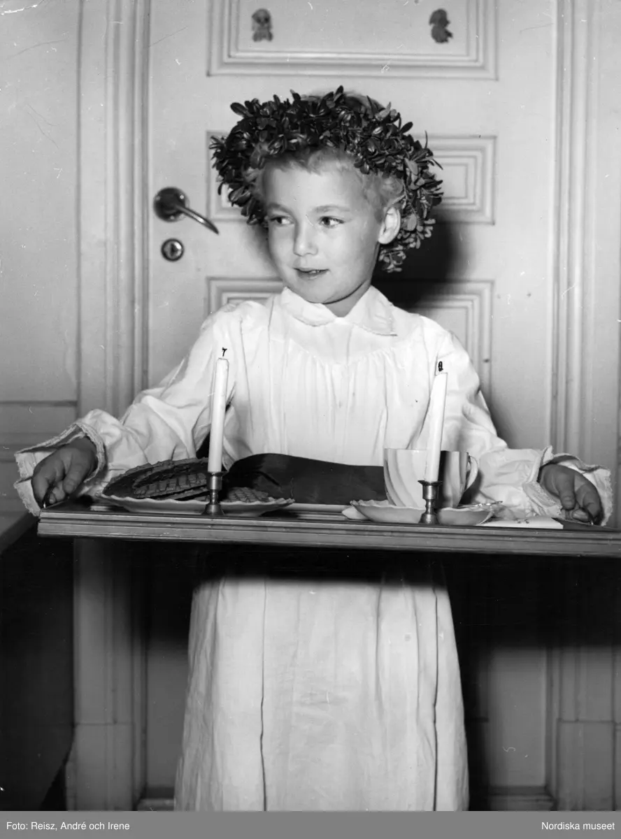 Luciafirande. En flicka i lucialinne och luciakrans bär en bricka ...