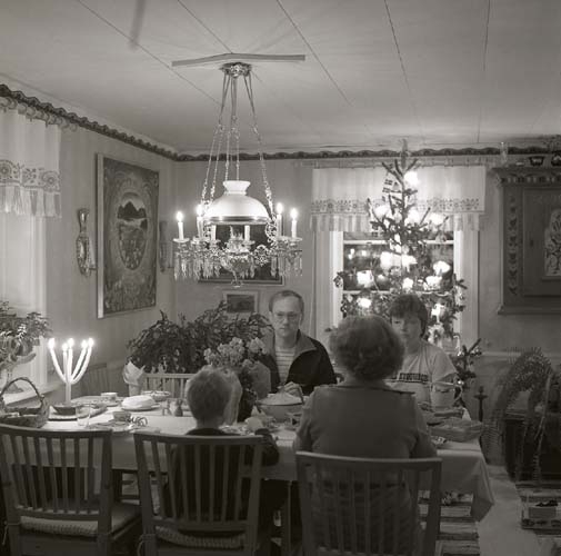 Fyra personer sitter runt ett fint dukat bord med tända ljus. I ...