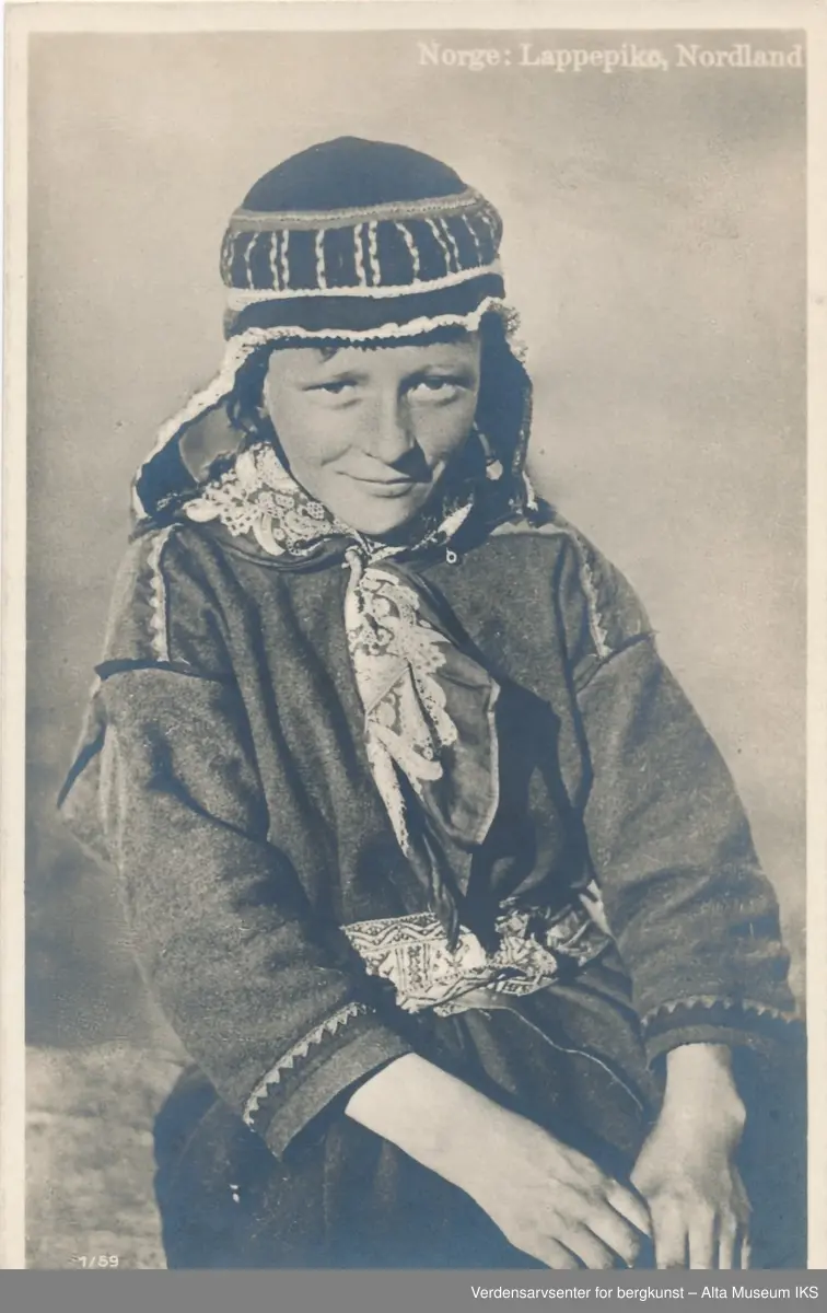 Samisk jente som smiler og ser mot kamera. Hun er ikledd kofte og lue ...